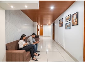 Um corredor com um banco marrom, paredes brancas e obras de arte emolduradas à direita.