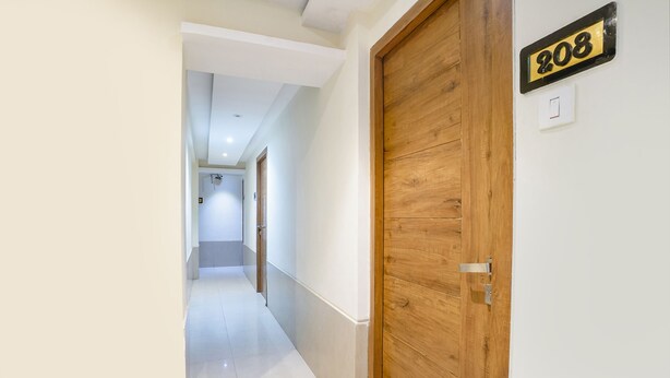 Um corredor com uma porta de madeira identificada com o número '208' e um interruptor de luz na parede.