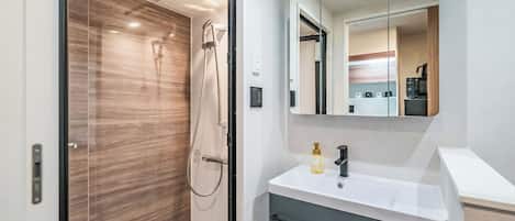 Uma casa de banho moderna com chuveiro, pia e espelho.