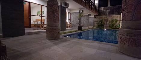 Área de piscina com pilares de pedra, um deck de madeira e um espaço de estar com mesas e cadeiras.