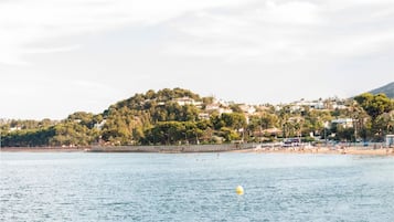 Vista costeira com praia, colina com edifícios e céu claro.