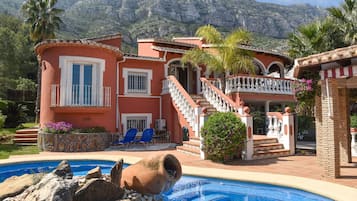 Uma casa de dois andares com piscina, escadaria e vista para montanhas.