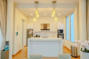 Uma cozinha moderna com armários brancos, uma ilha central, luminárias pendentes e vista da cidade.