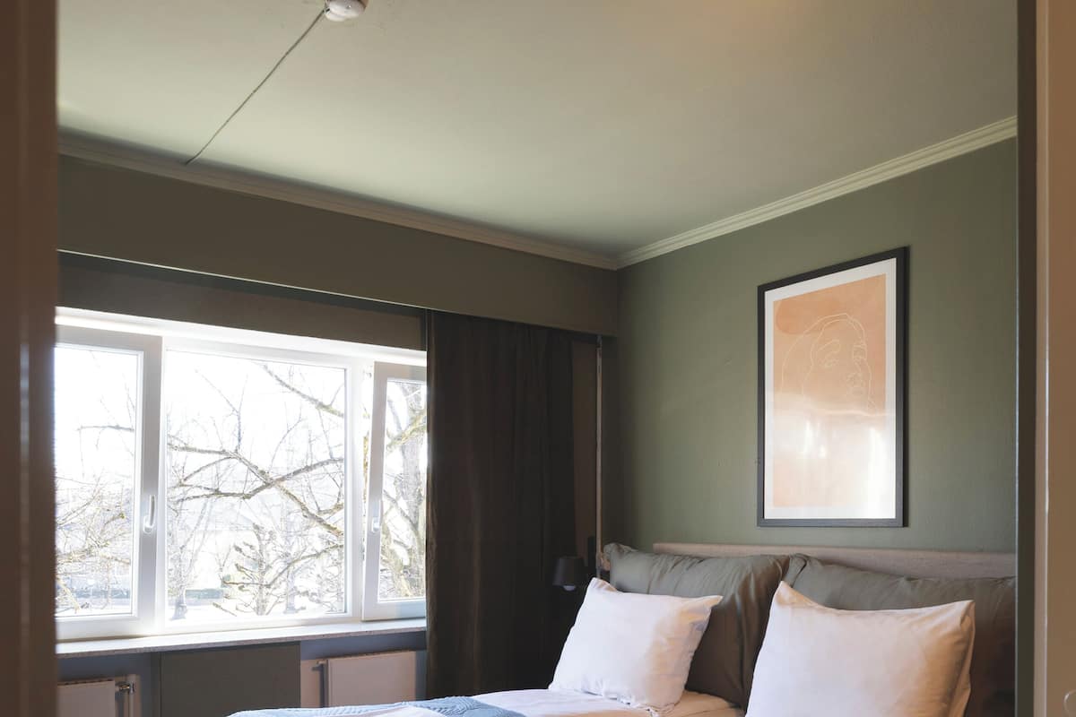Uma cama de casal com cabeceira, uma janela com cortinas e um quadro na parede.