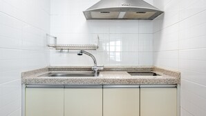 Uma cozinha com paredes revestidas de azulejos brancos, uma pia de aço inoxidável e um exaustor embutido.