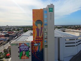 Um hotel com um grande mural na fachada, uma placa para 'Green Life Academias' e vista para a paisagem urbana ao redor.