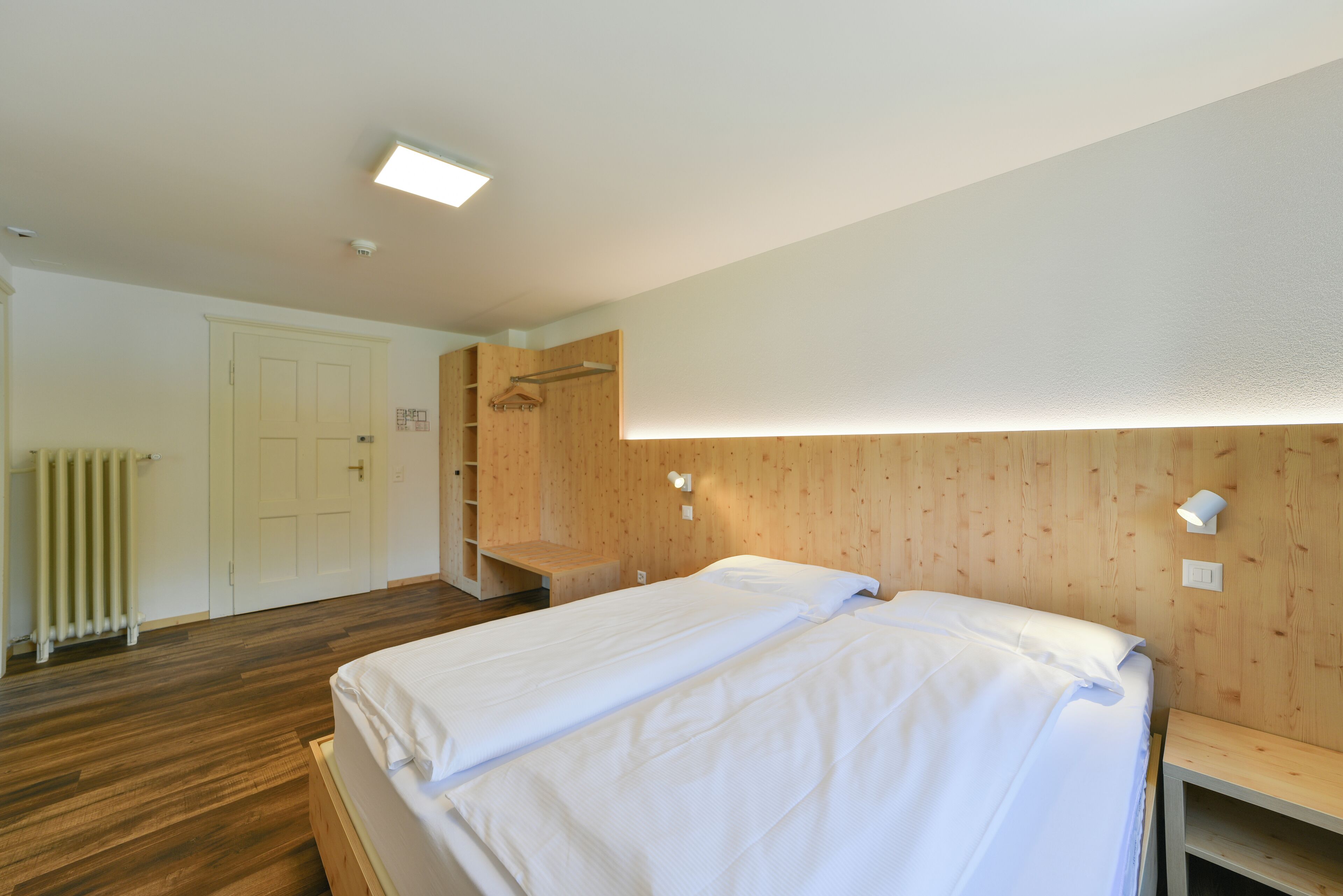 Quarto com cabeceira de madeira, cama com lençóis brancos, mesa de cabeceira de madeira e prateleira embutida.
