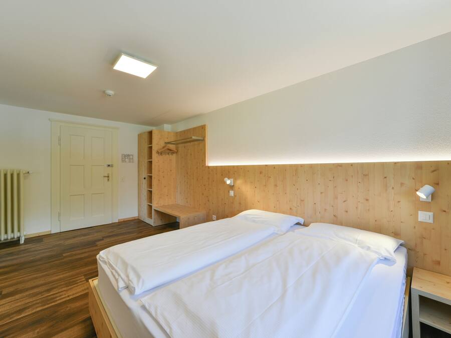 Quarto com cabeceira de madeira, cama com lençóis brancos, mesa de cabeceira de madeira e prateleira embutida.