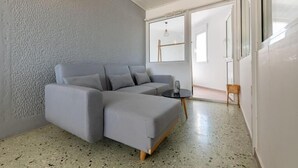 Uma sala de estar moderna com um sofá seccional cinza, uma mesa redonda pequena e uma janela com vista.