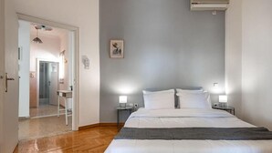Quarto com cama, mesas de cabeceira, ar condicionado e porta para outro espaço.