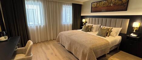 Quarto de hotel com uma cama grande, uma escrivaninha e uma cadeira. Há duas mesas de cabeceira com luminárias.