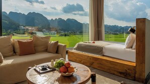 Quarto de hotel moderno com uma janela ampla que oferece uma vista panorâmica de montanhas e um vale verde.