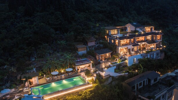 Uma casa grande, com vários andares, e uma piscina, cercada por vegetação exuberante.