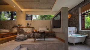 Uma casa de banho moderna com parede de pedra, banheira, lavatório e janela com vista para vegetação.