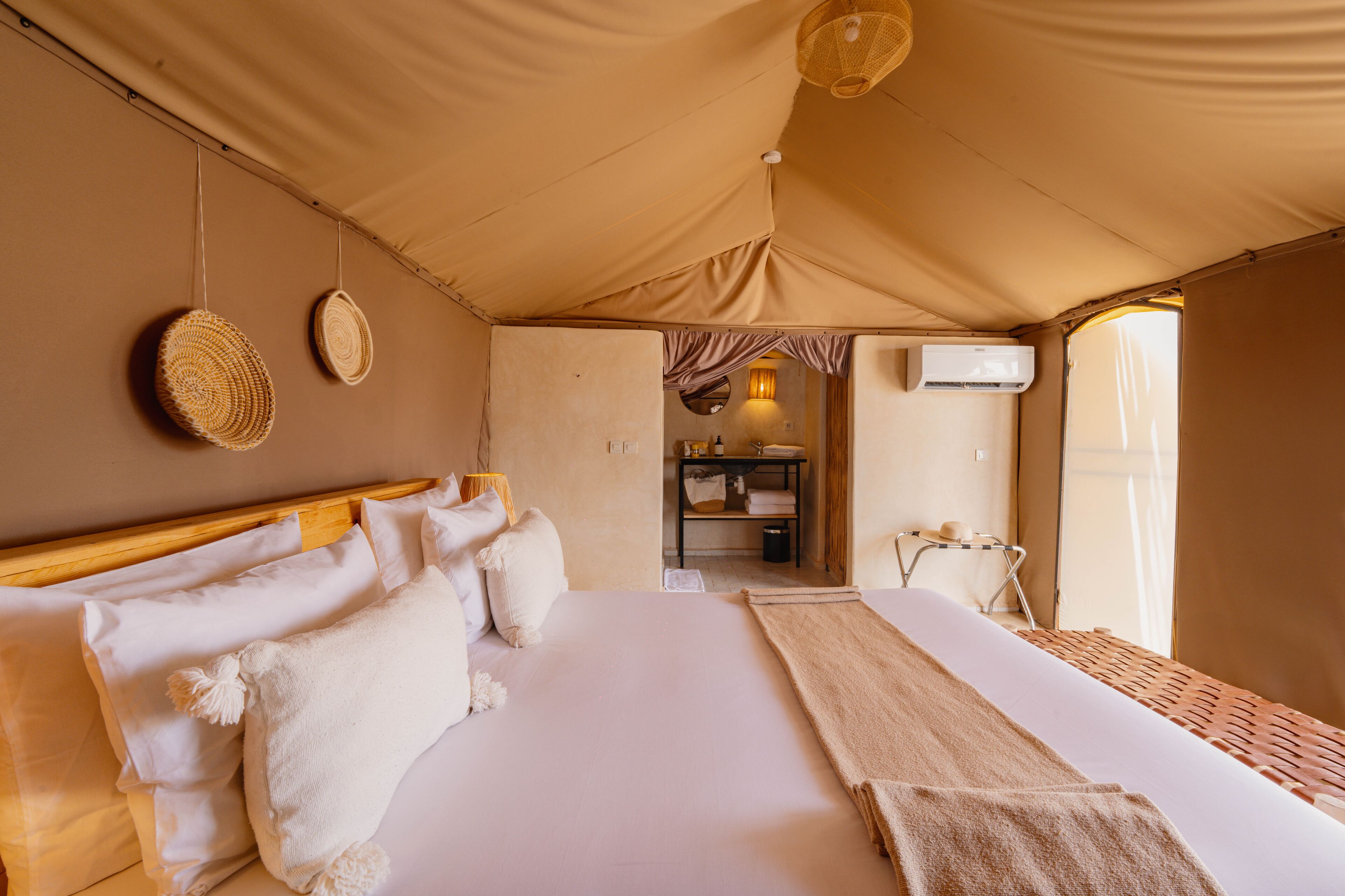 Quarto com tenda, uma cama, almofadas, cesto pendurado e aparelho de ar condicionado.