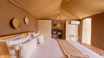 Quarto com tenda, uma cama, almofadas, cesto pendurado e aparelho de ar condicionado.