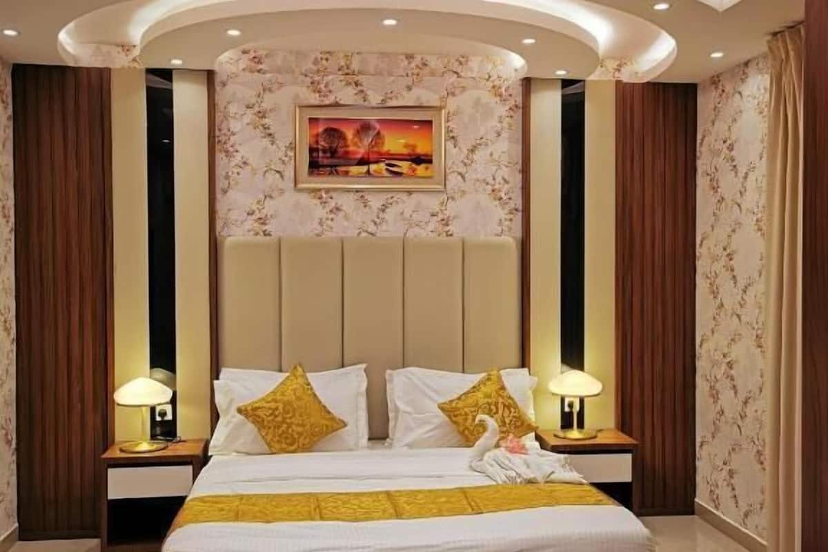 Quarto de hotel moderno com uma cama grande, duas mesas de cabeceira com luminárias, um banco e um quadro na parede.