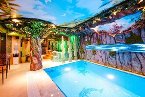 Piscina interna com tema tropical, incluindo uma grande árvore e formações rochosas.