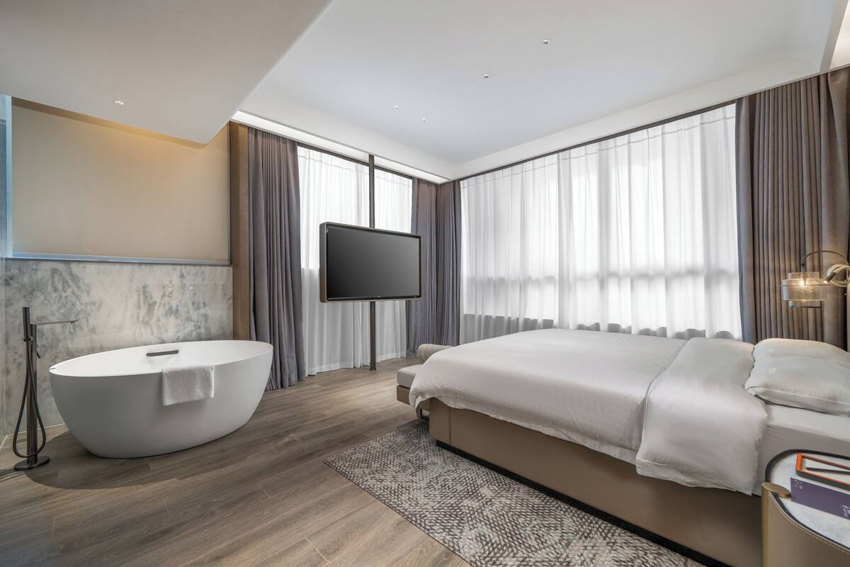 Quarto de hotel moderno com uma cama grande, uma banheira e uma televisão de tela plana.