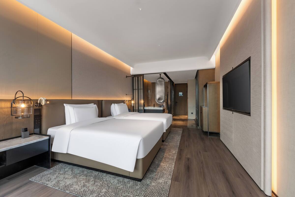 Quarto de hotel moderno com uma cama grande, mesas de cabeceira, televisão e espelho.