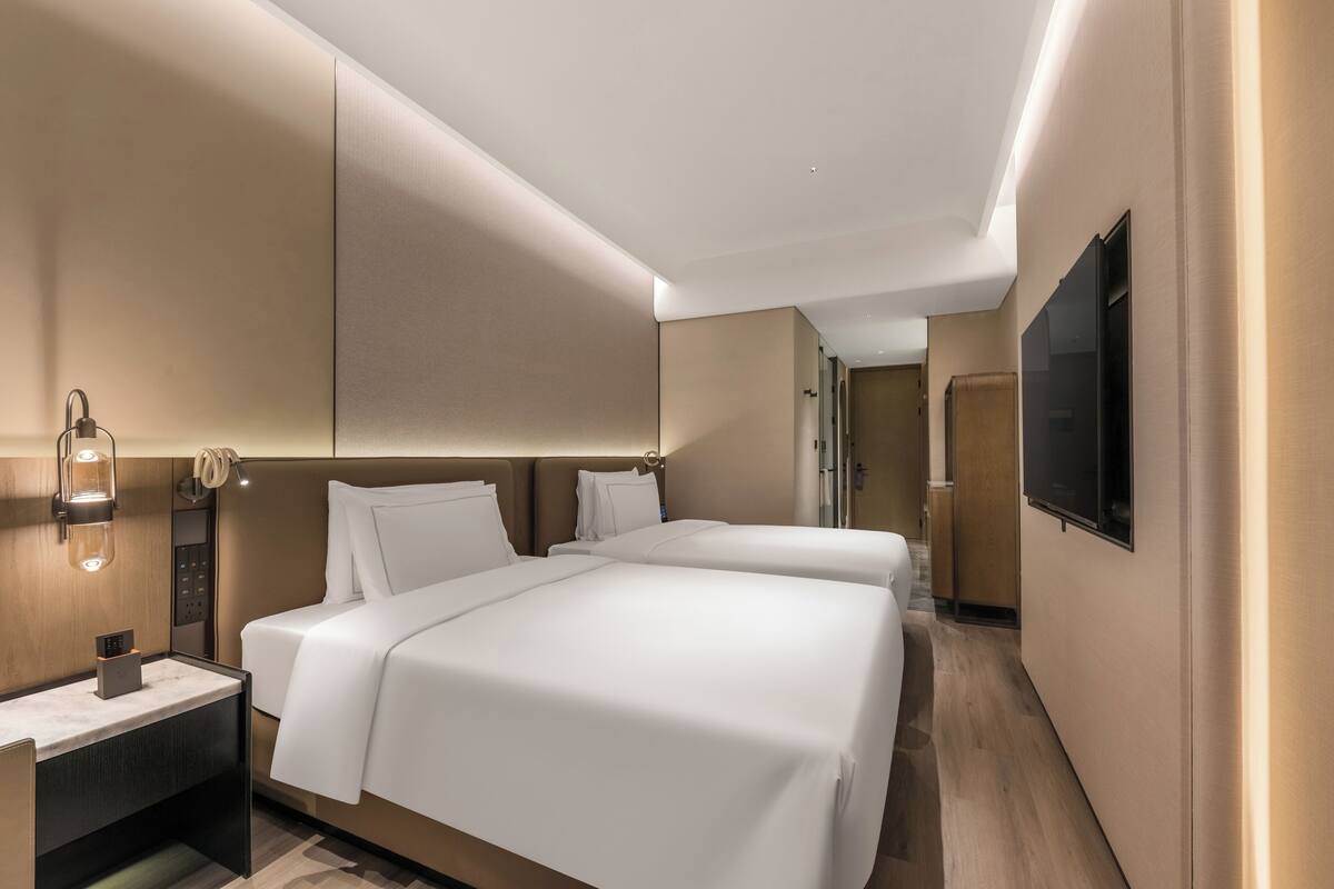 Quarto de hotel com duas camas, televisão, secretária com candeeiro e minibar.