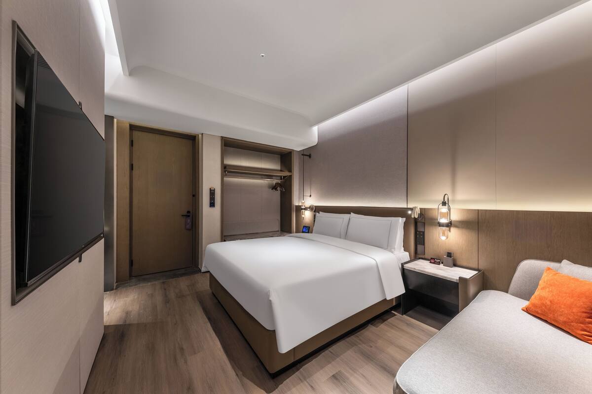 Quarto de hotel moderno com uma cama grande, mesas de cabeceira, uma TV e um guarda-roupa.