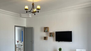 Uma sala de estar moderna com um sofá, uma mesa de centro, uma TV na parede e uma cadeira branca pequena.