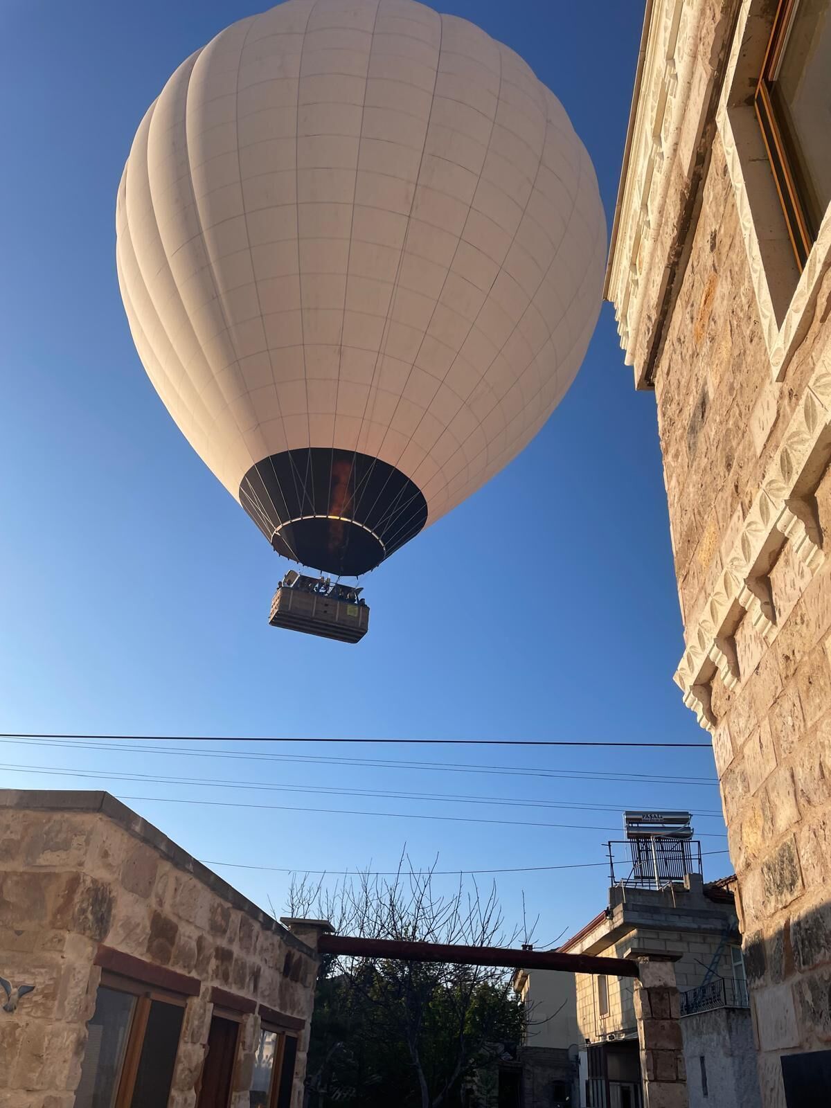 Um balão de ar quente com uma cesta, voando sobre um edifício de pedra com uma placa que diz 'VASAL'.