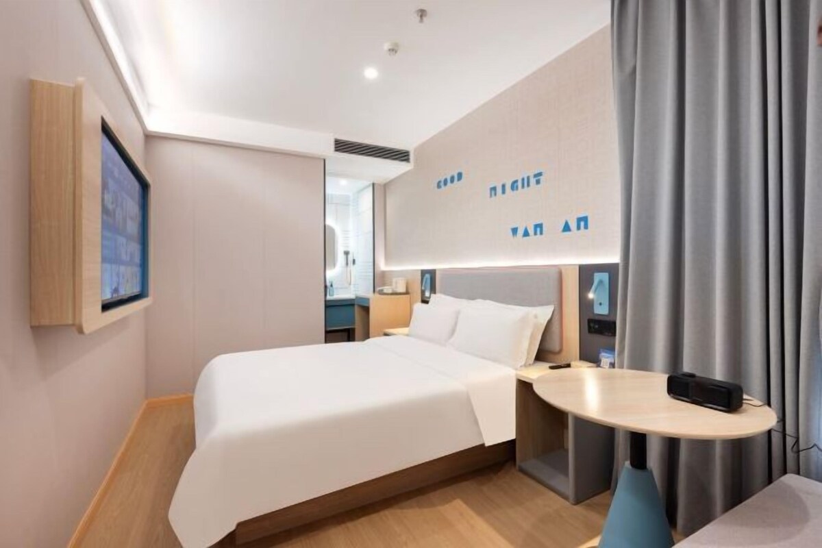 Quarto de hotel com cama, mesa de cabeceira e uma mesinha com telefone.