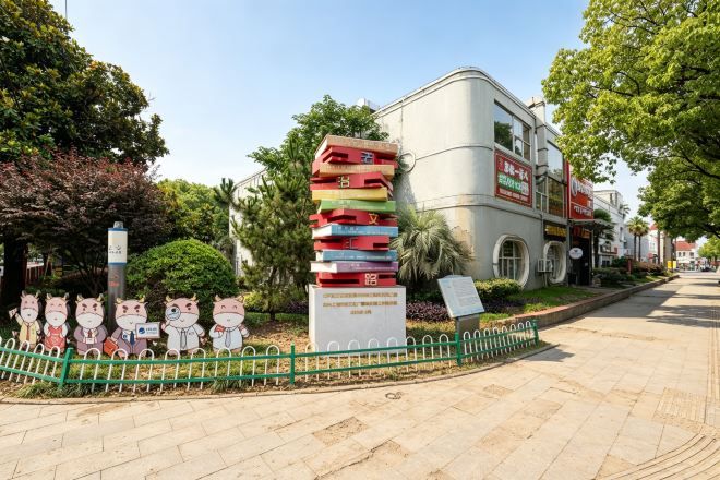 Um edifício com uma pilha de livros coloridos, uma cerca verde e figuras de porcos em desenho animado.