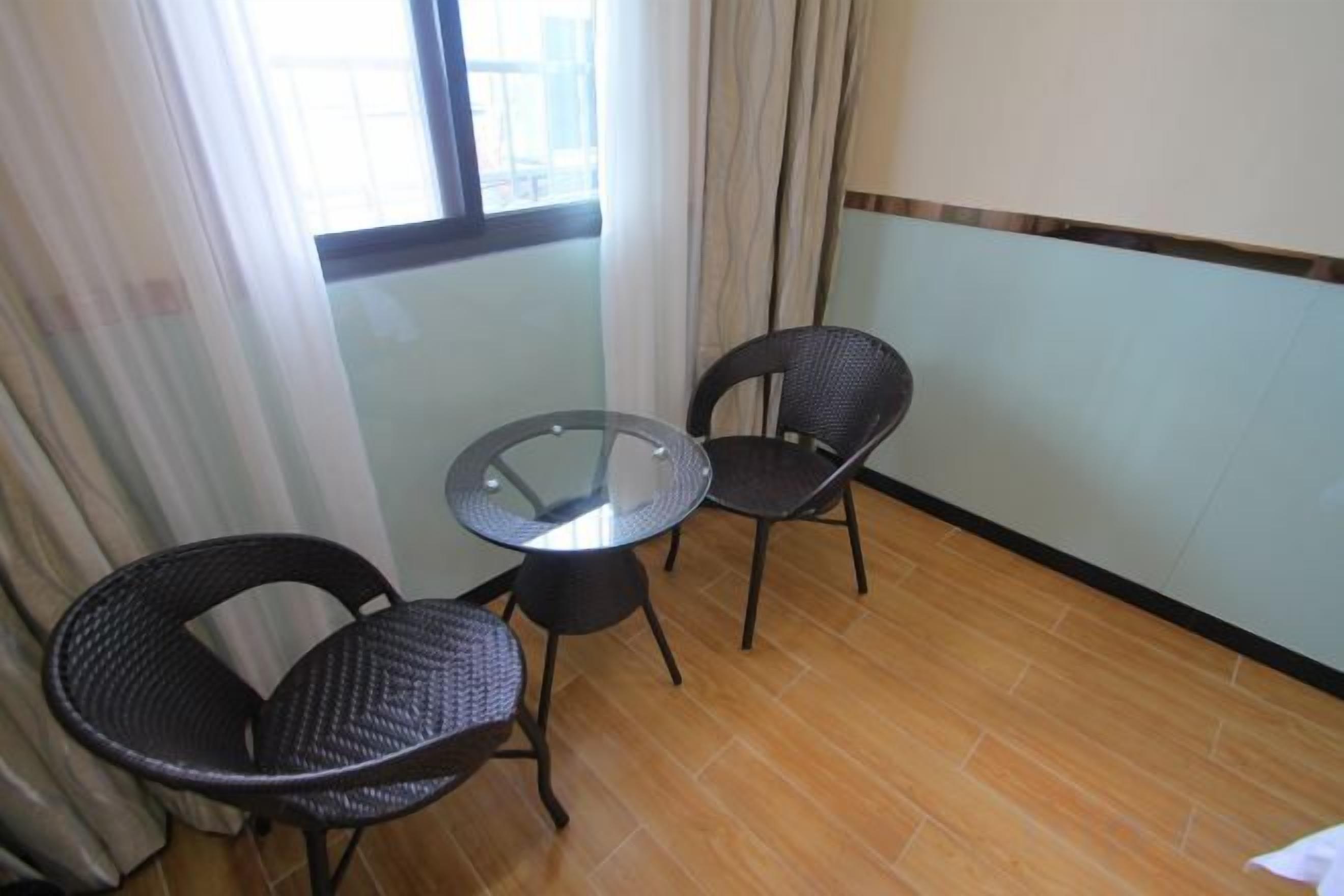 Um quarto pequeno com uma mesa de vidro e duas cadeiras, uma janela com cortinas e piso de azulejos.