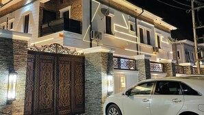 Uma casa moderna de dois andares com portão fechado, um carro branco estacionado em frente e fachada bem iluminada.