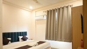 Quarto de hotel com uma cama, cabeceira de madeira, TV de tela plana e janela com cortinas.
