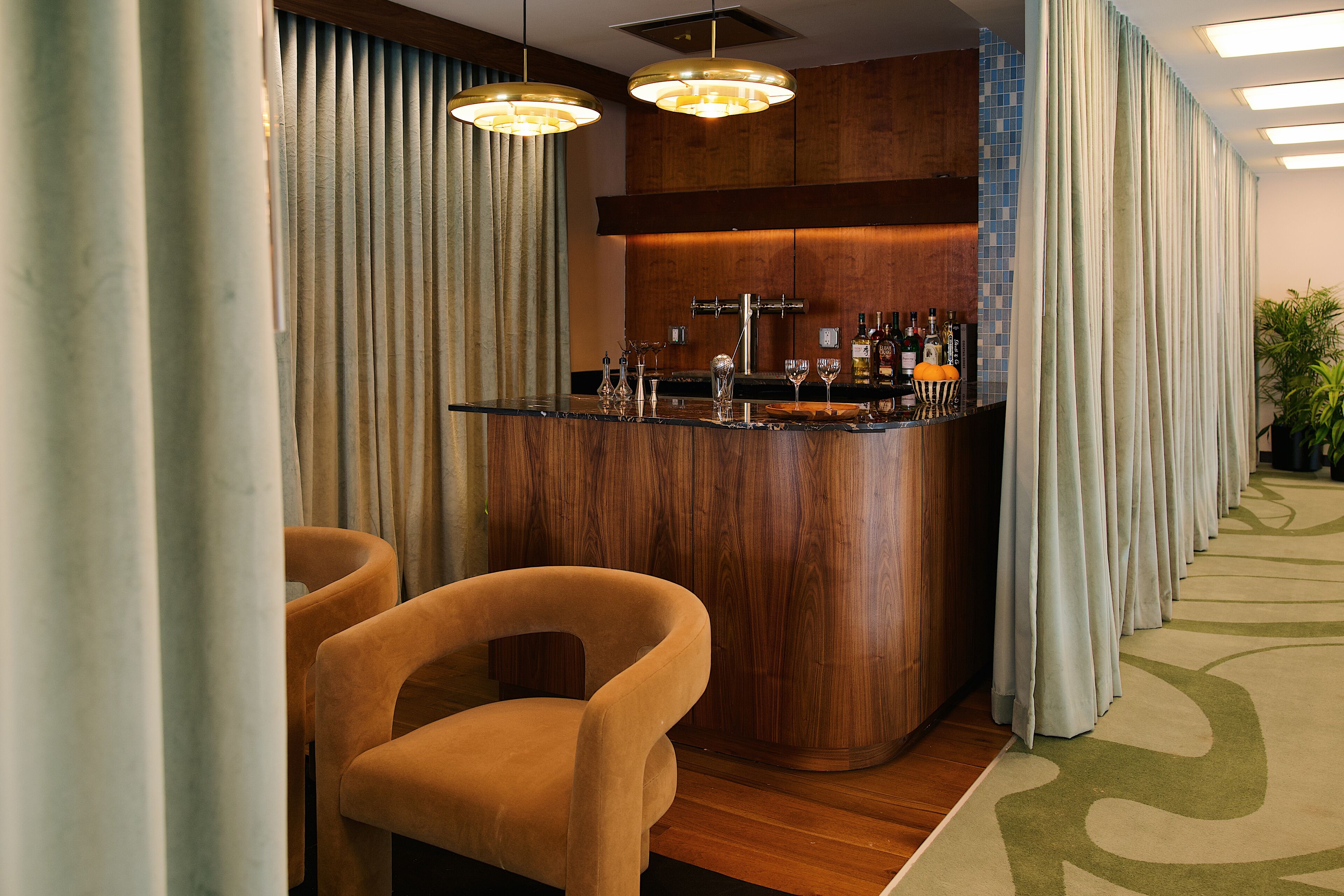 Uma área de bar com balcão de madeira, banquetas e painel de azulejos.