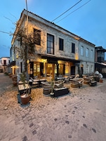 Um edifício de dois andares com um café no andar térreo, mesas ao ar livre e calçada de pedra.