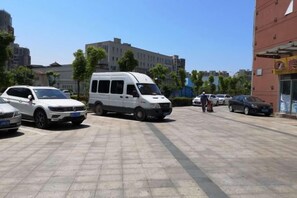 Um estacionamento com vários veículos, incluindo uma van branca e diversos carros.