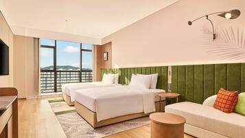Quarto de hotel moderno com uma cama grande, um sofá, uma escrivaninha e vista para a paisagem urbana.