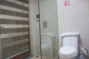 Casa de banho com chuveiro em cabine de vidro, sanita branca e um contentor de lixo.