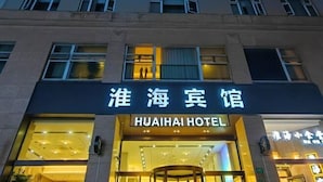 Exterior do HOTEL HUAIHAI, com letreiros iluminados e fachada moderna.