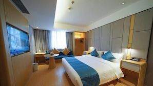 Quarto de hotel moderno com uma cama grande, televisão, secretária e área de estar confortável.