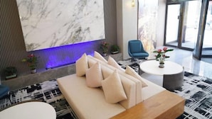 Um lobby moderno com uma parede de mármore, uma área de estar com almofadas, uma mesa redonda e uma cadeira azul.