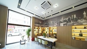 Um lobby de hotel moderno com um mural da cidade, um balcão de recepção e uma área de estar com mesa e cadeiras.