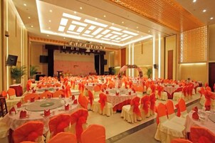 Uma sala de banquetes com mesas redondas e cadeiras, um palco e uma tela grande.