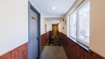 Um corredor de hotel com piso de madeira, uma porta à esquerda e janelas à direita.