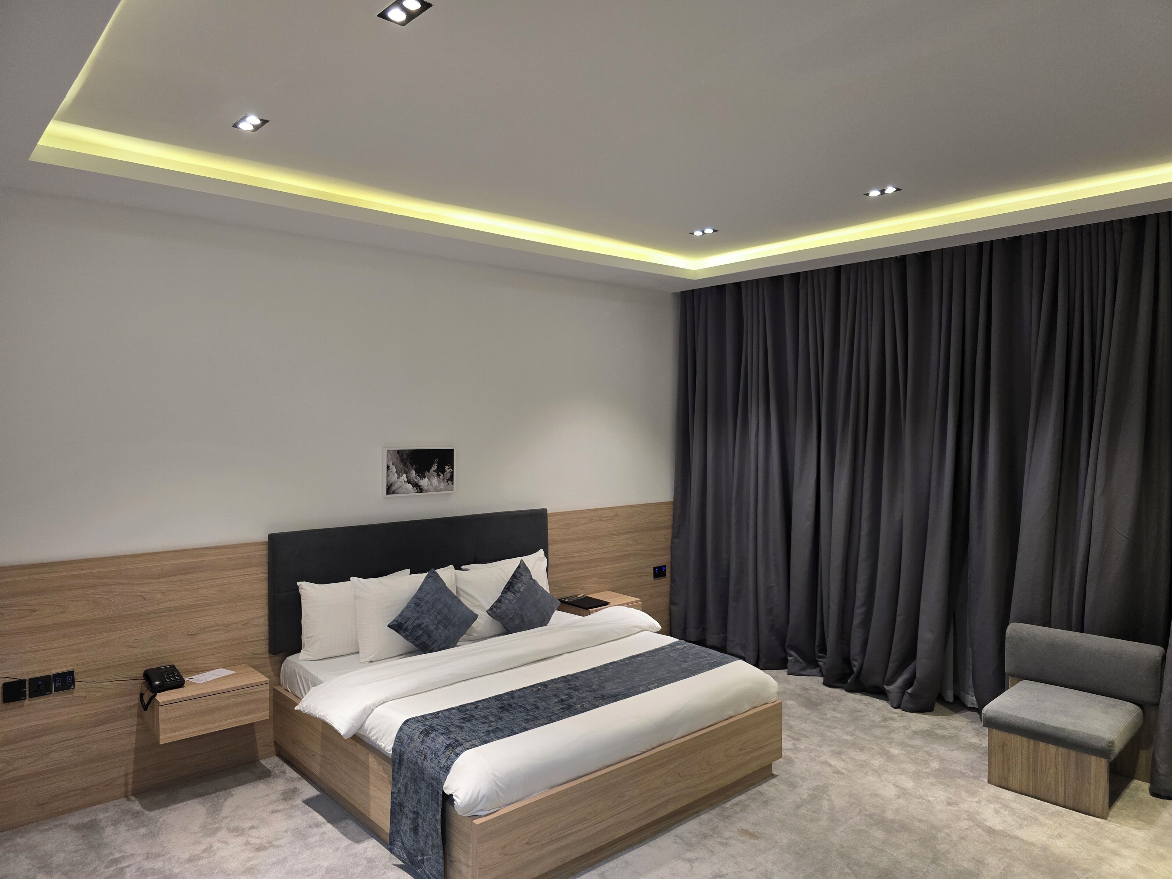 Quarto moderno com cama de madeira, mesa de cabeceira com telefone e um pequeno espaço de estar.