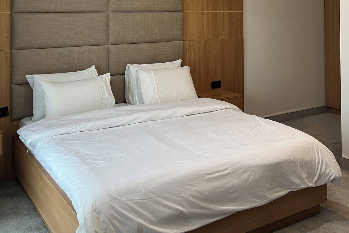 Quarto moderno com uma cama grande, cabeceira acolchoada e parede de destaque em madeira.