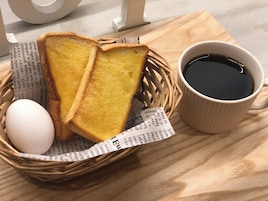 Uma cesta com duas fatias de torrada, um ovo cozido e uma xícara de café preto sobre uma bandeja de madeira.
