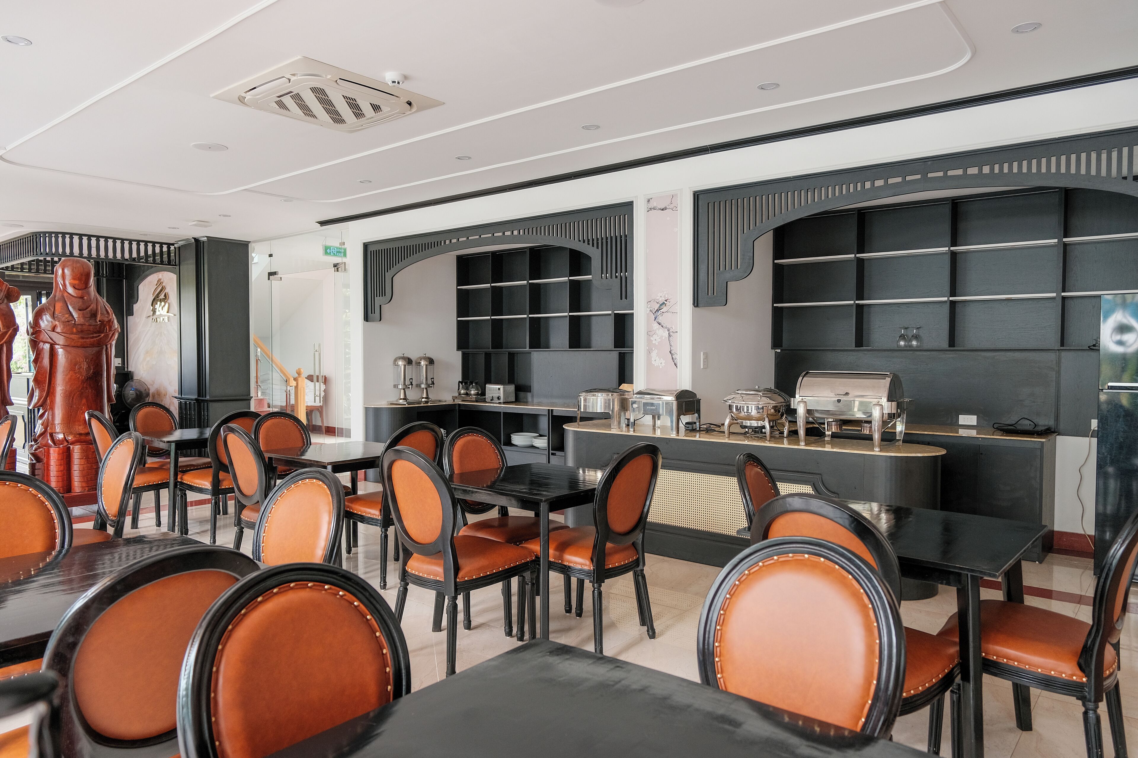 Um restaurante moderno com cadeiras pretas e laranja, um balcão central e uma estátua decorativa.