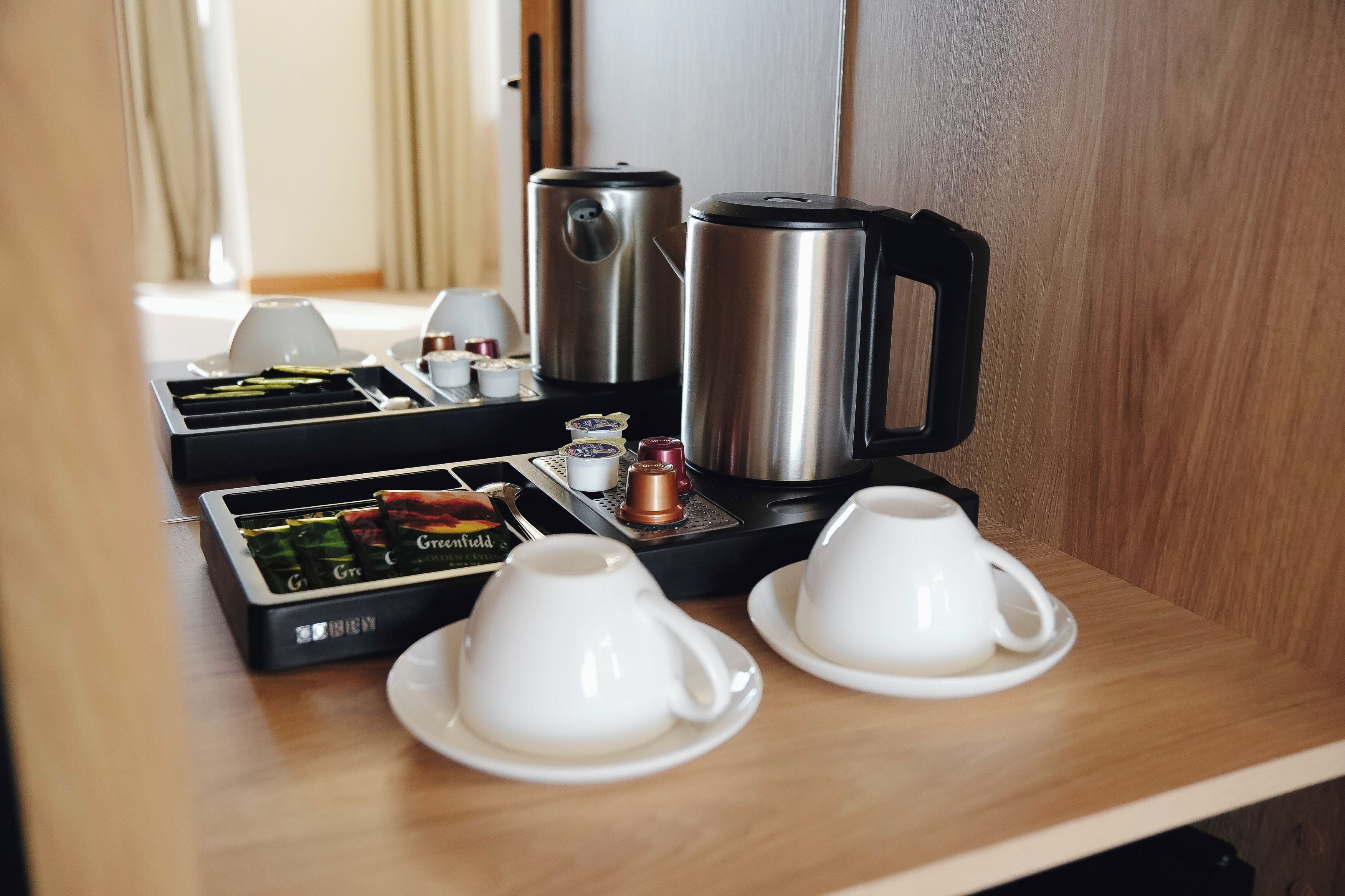Disposição para o café da manhã, com uma cafeteira, duas xícaras e um conjunto de chá sobre uma mesa de madeira.