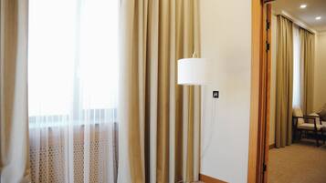 Quarto de hotel com abajur, cortinas bege e piso coberto por carpete.